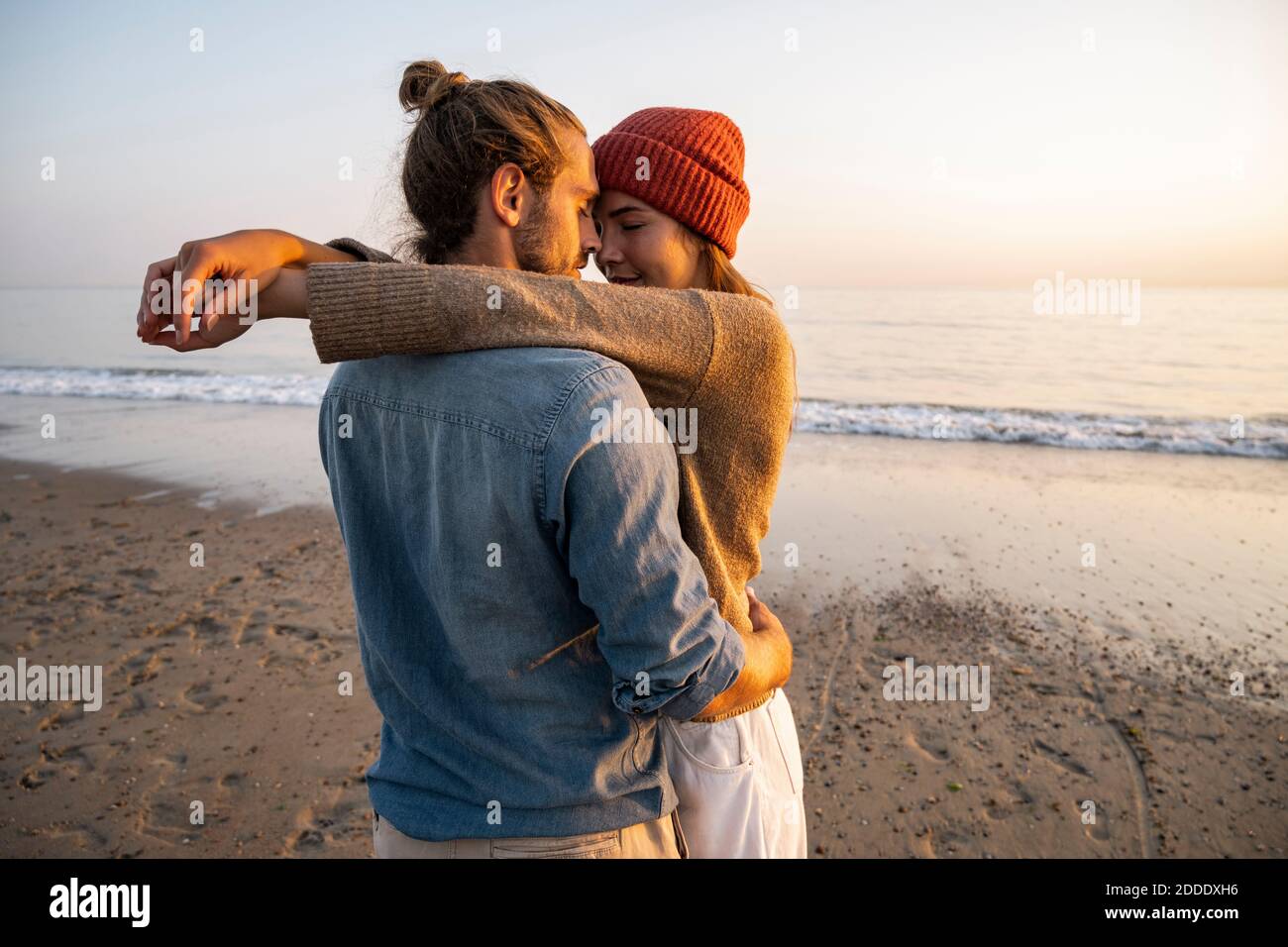 Young romantic couple standing face to face at beach against clear sky ...