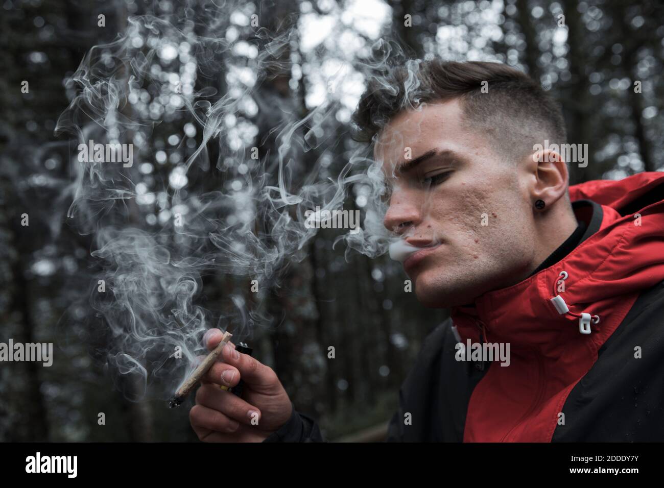 Young man smoking cigarette while standing in forest during autumn ...