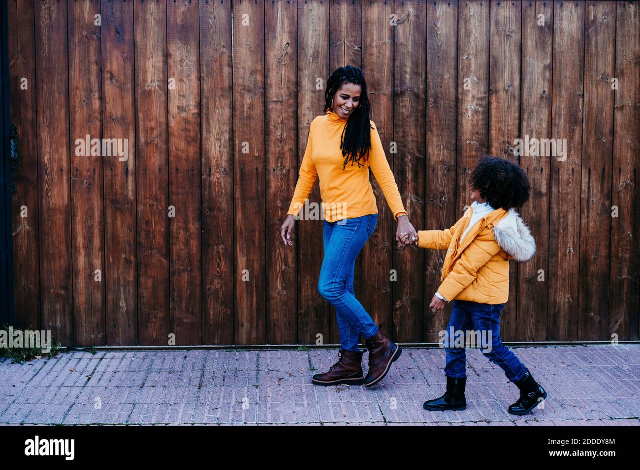 Mother holding daughter hand while walking against wooden wall Stock ...