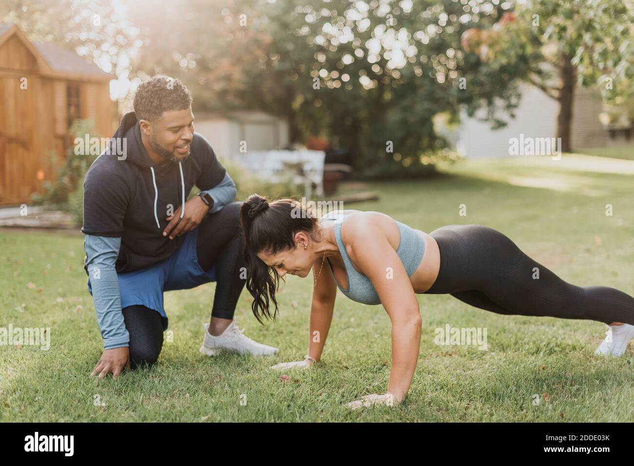 Smiling man looking at woman doing push ups at backyard Stock Photo - Alamy