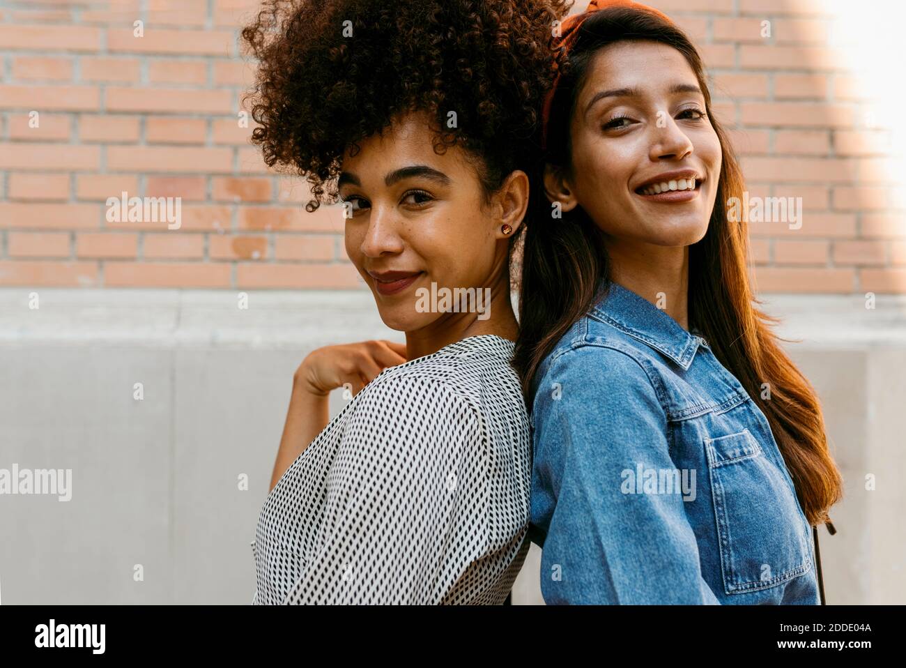 Friends standing back to back against wall Stock Photo - Alamy