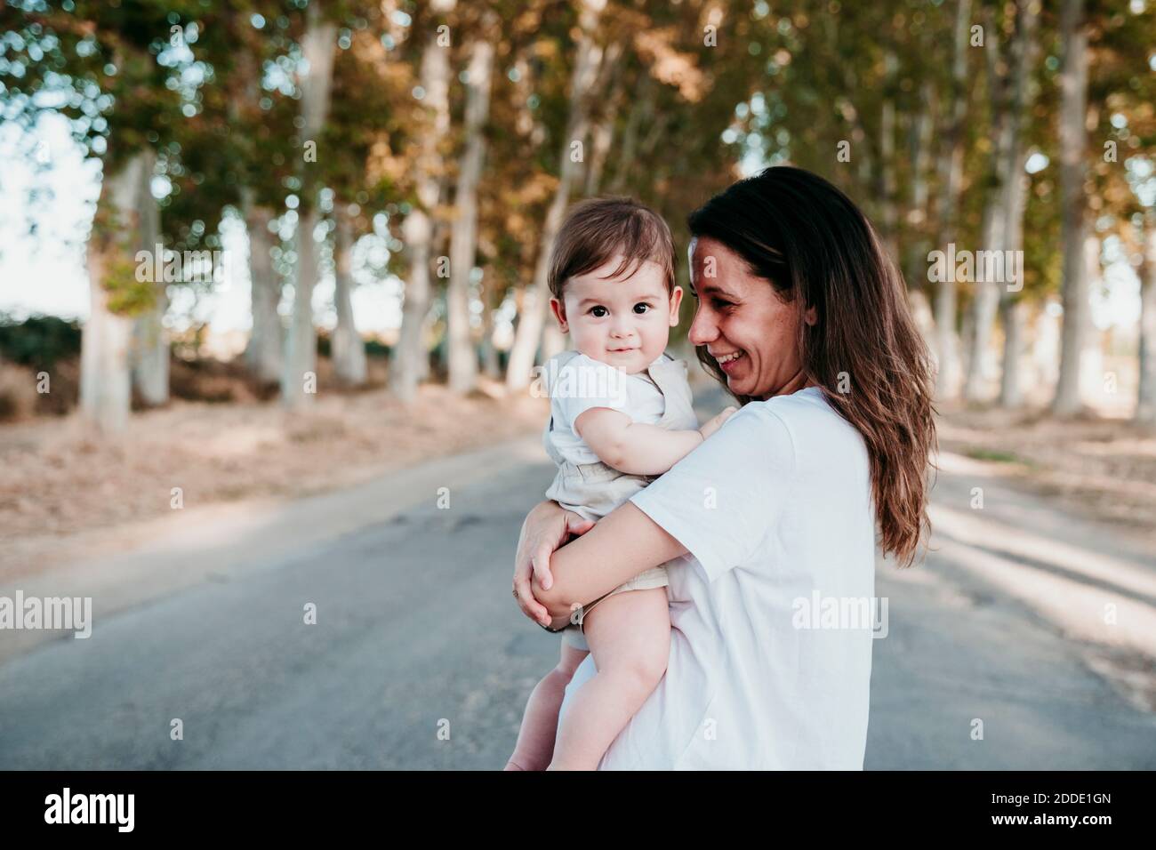 Smiling mother carrying baby boy while standing outdoors Stock Photo ...