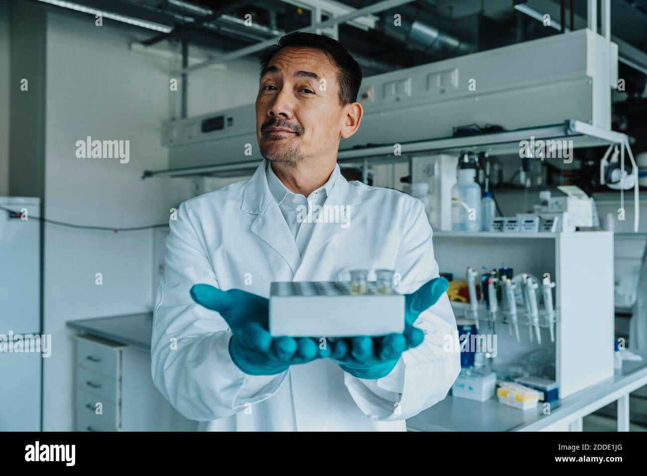 Confident scientist showing test tube tray while standing at laboratory ...