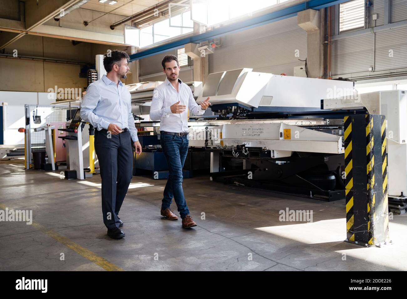 Business people discussing while walking by machine at factory Stock ...