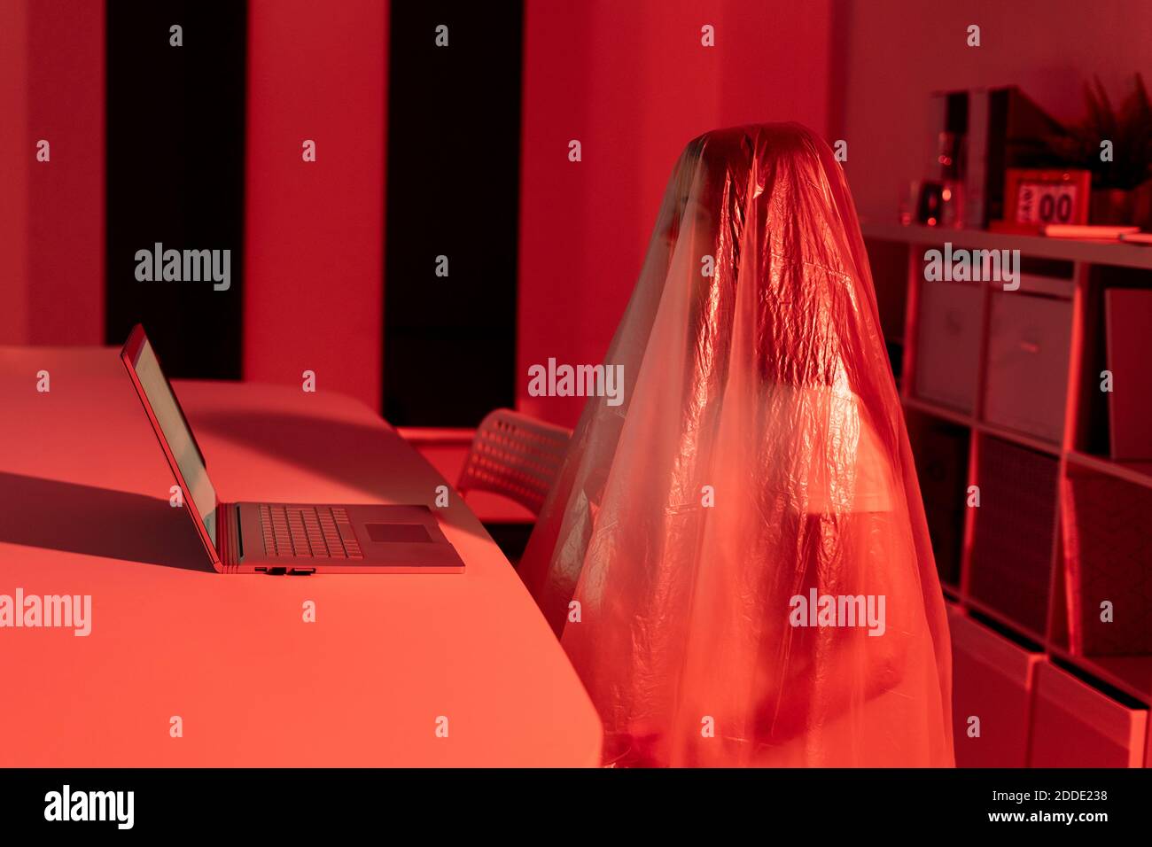 Young woman covered in plastic sitting with laptop at desk in home ...