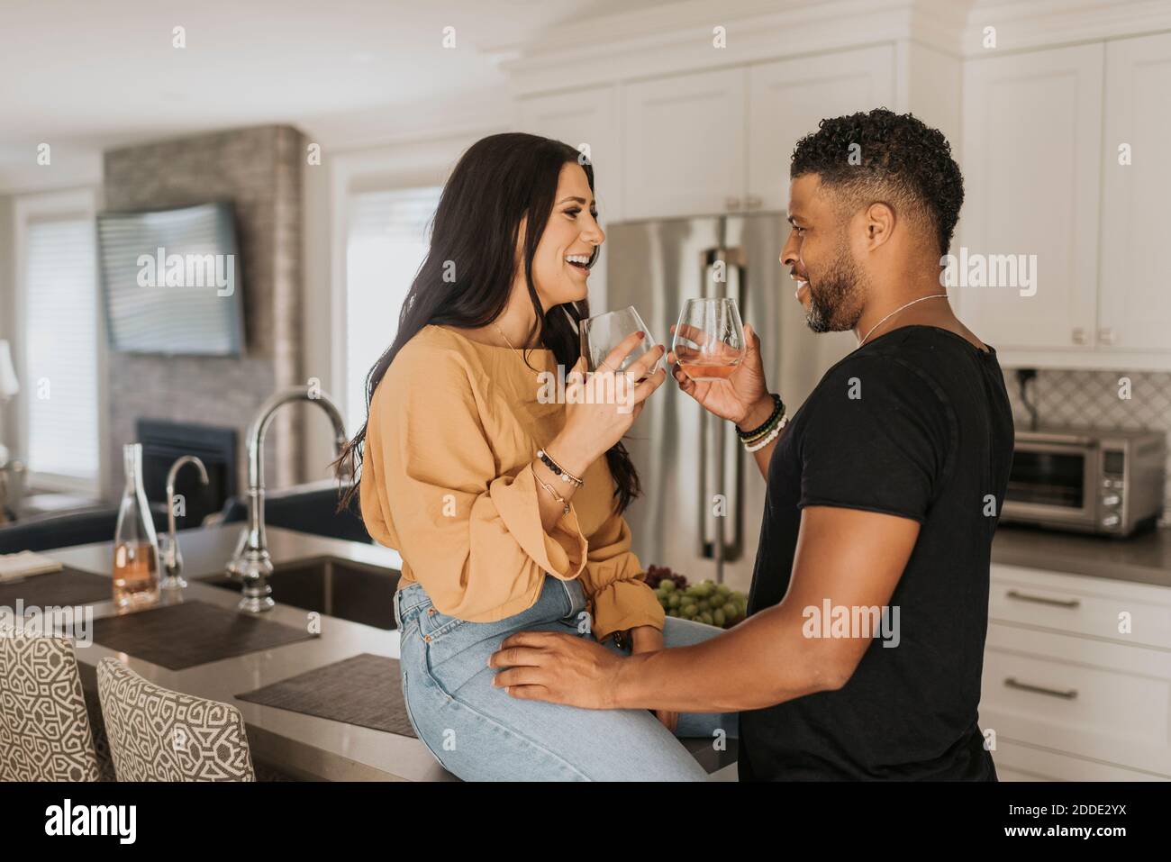 Mid adult man standing by woman sitting on kitchen counter at home ...