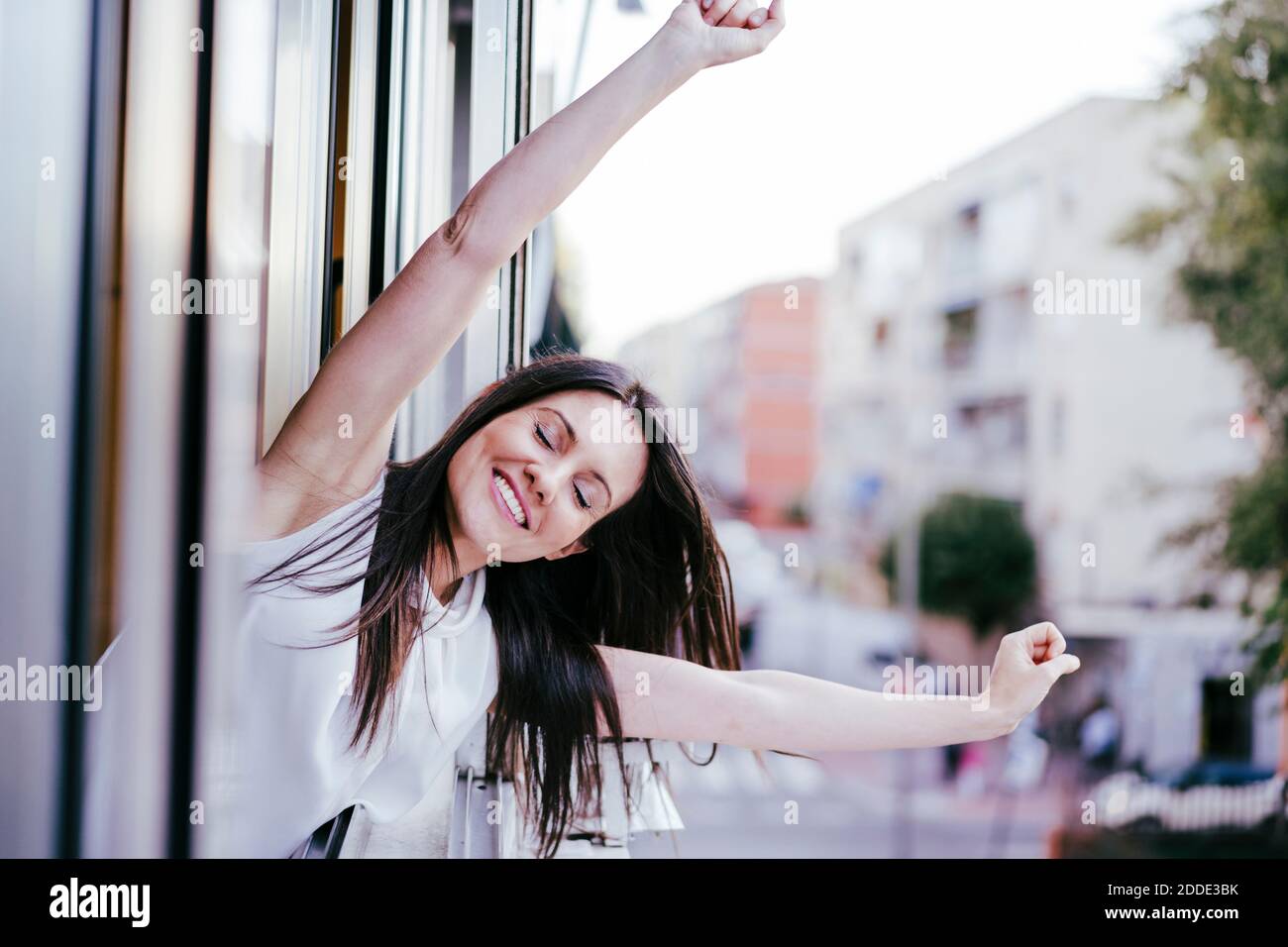 Woman with arms raised leaning out window while standing in house Stock ...