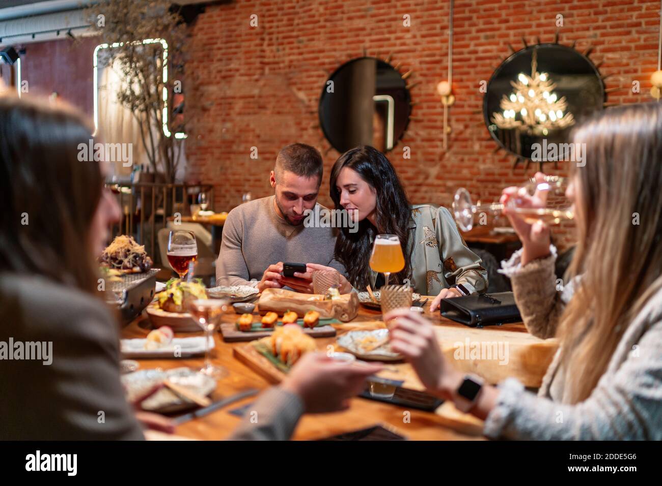 Women talking while drinking wine with friends using mobile phone in ...