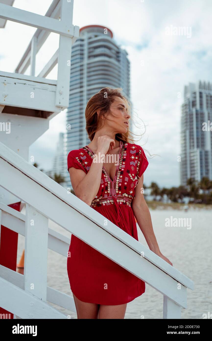 Beautiful woman wearing red dress leaning on wooden structure of ...