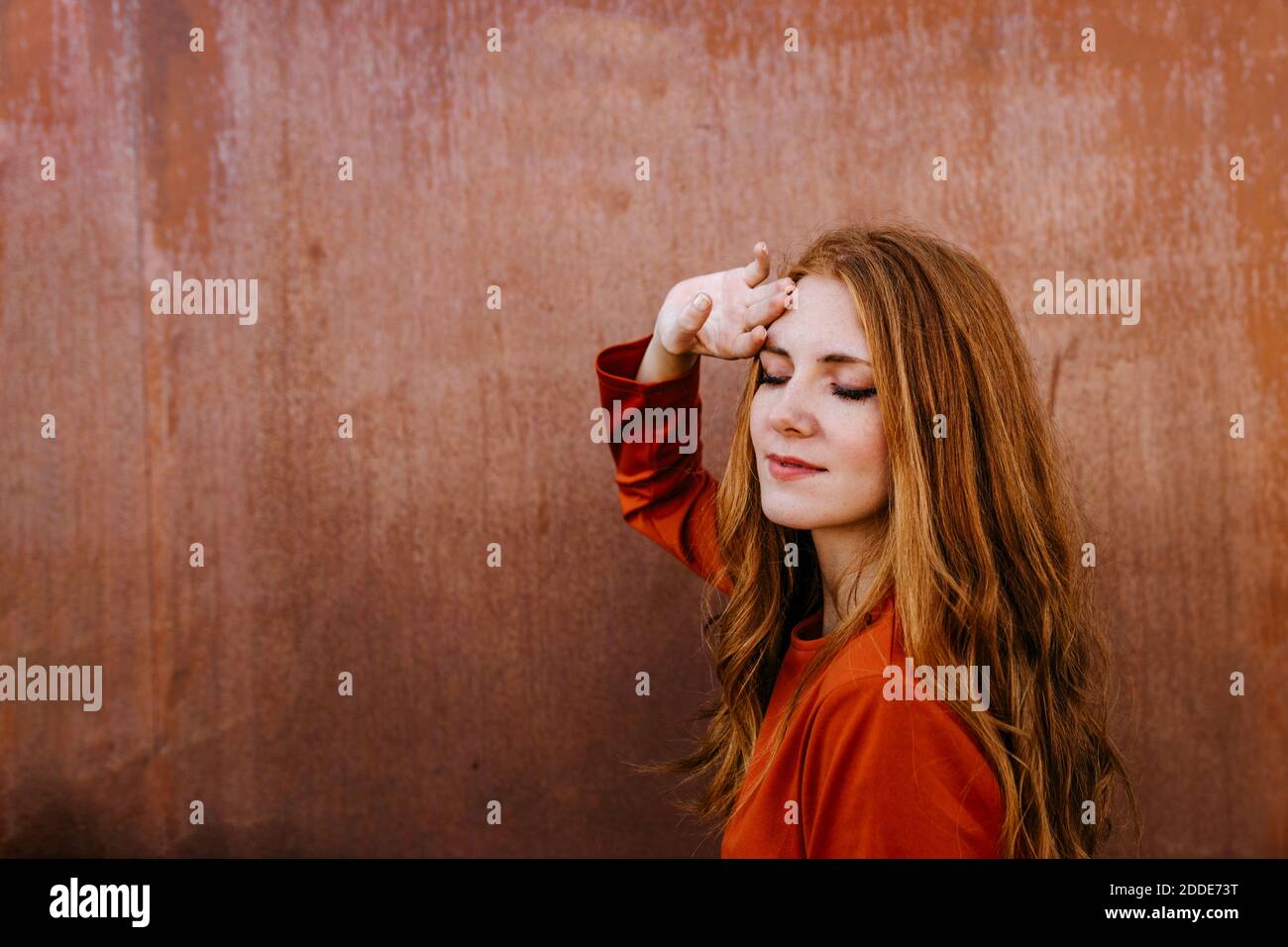 Beautiful woman touching forehead in front of brown wall Stock Photo ...