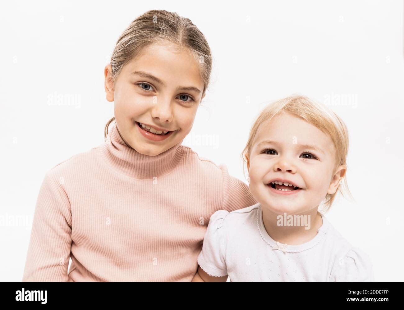 Smiling sisters sitting against white background in studio Stock Photo ...