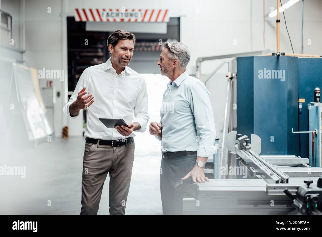 Mature businessman explaining colleague while standing in manufacturing ...