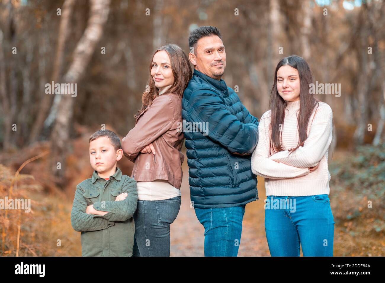 Parents standing back to back along with children arms crossed in park ...