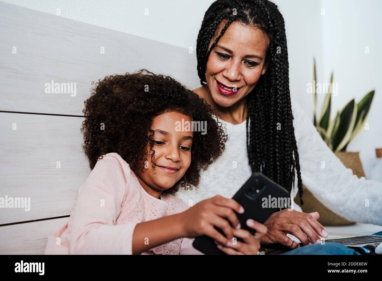 Daughter text messaging on smart phone with mother on bed in bedroom at ...