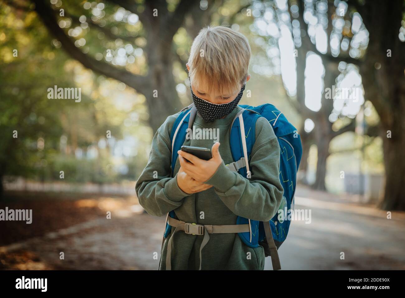 Boy text messaging on smart phone wearing protective face mask while ...
