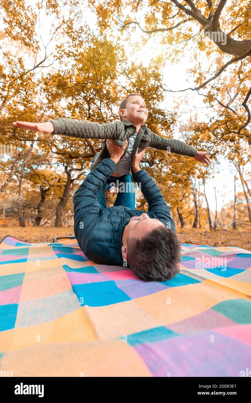 Boy imagining himself flying held by father lying on picnic blanket at ...