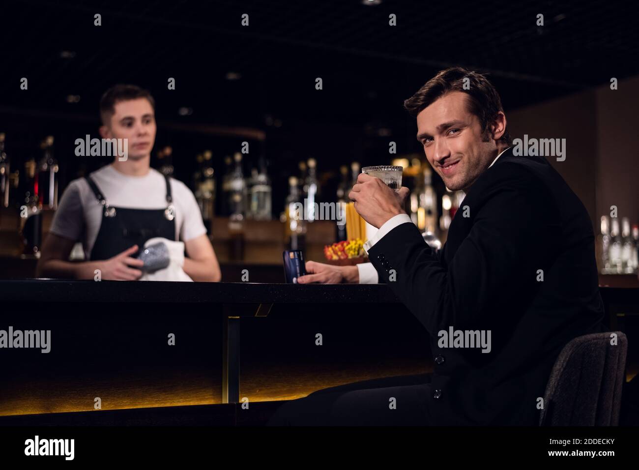 a handsome man poses at the bar with a cocktail in his hands against ...