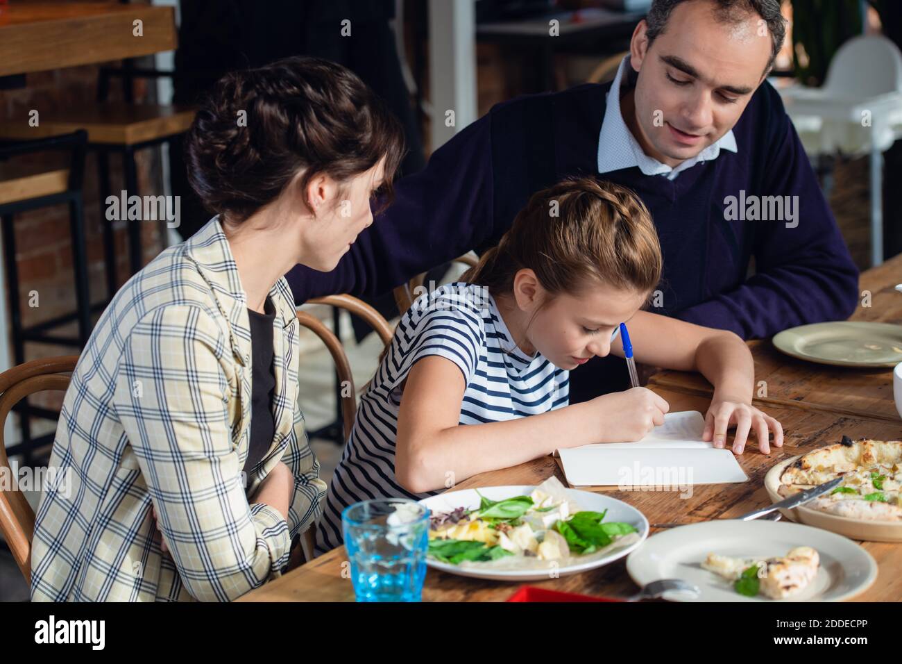 A girl doing her homework at the kitchen table with her parents being ...
