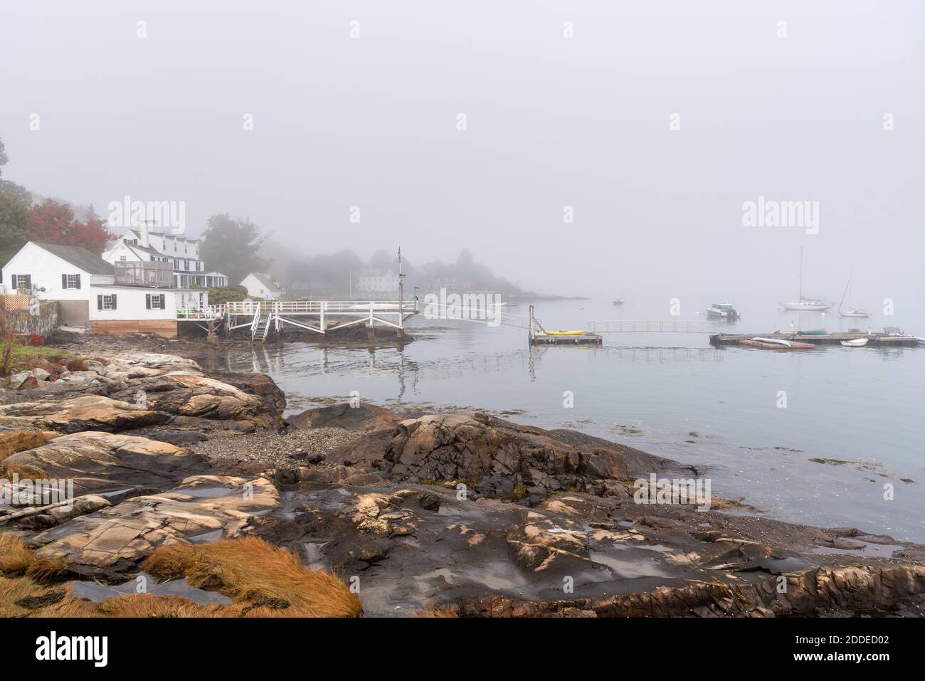 Bay shrouded in morning fog with anchored boats and wooden jetties in ...