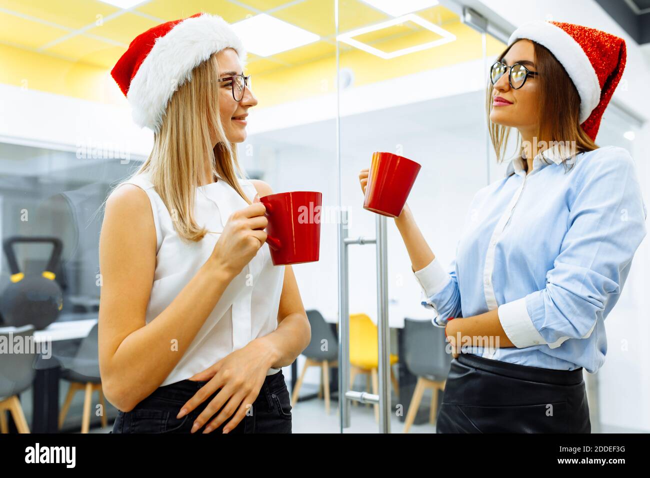 young business women in santa claus hats drinking tea or coffee during ...