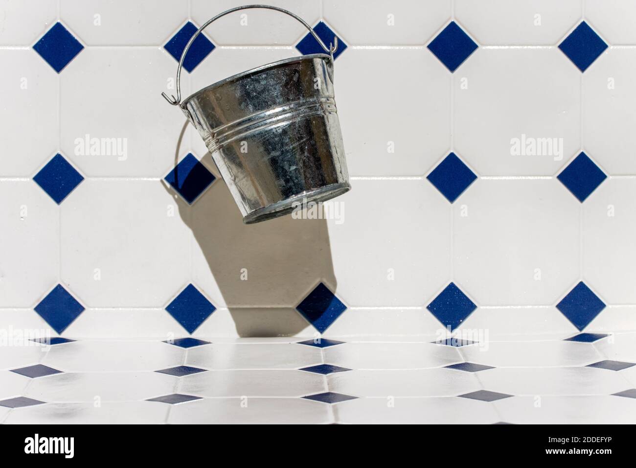 A metal bucket falling on white tiles Stock Photo - Alamy