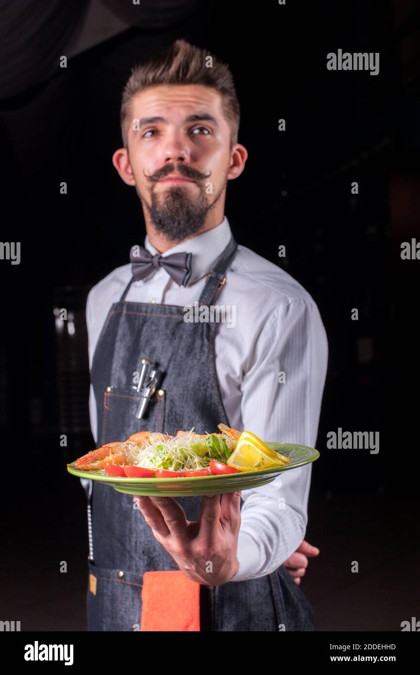 Professional friendly waiter helpfully holds salad in the restaurant ...