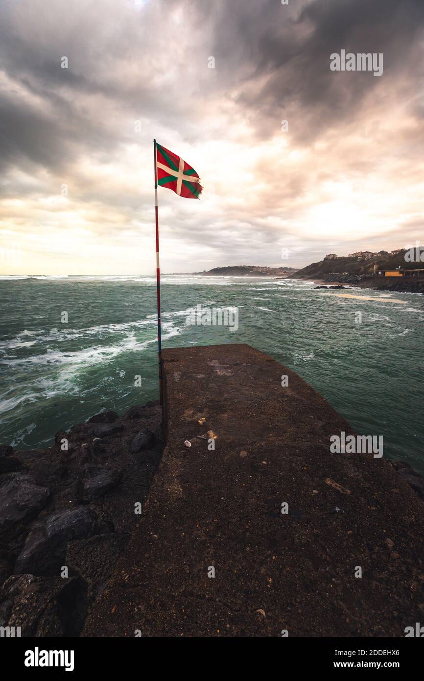 Basque national flag (Ikurriña) at the edge of a pier on the coast ...