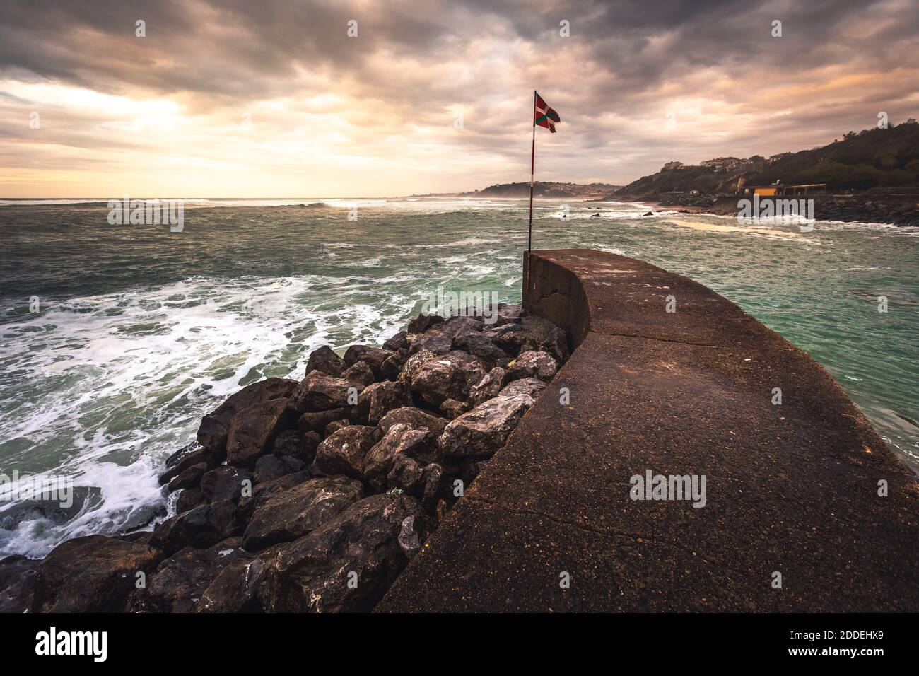 Basque national flag (Ikurriña) at the edge of a pier on the coast ...