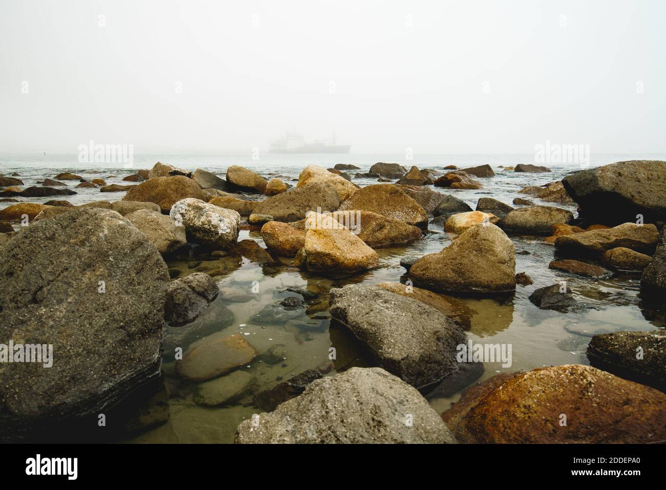 Quiet water, seashore rocks, and silhouette of vessel on a horizon at ...