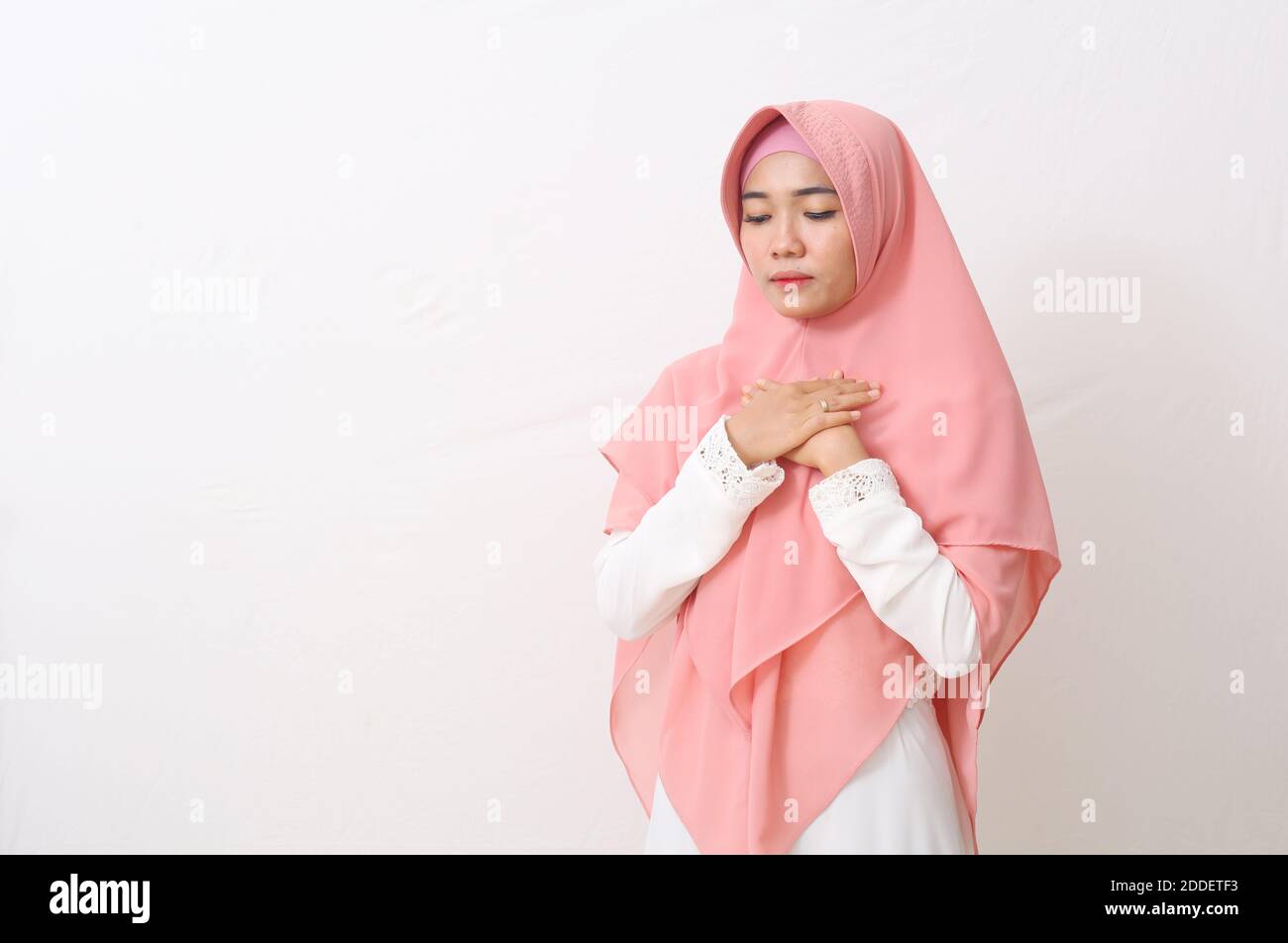 Faithful asian muslim woman closes eyes and keeps hands on chest near ...