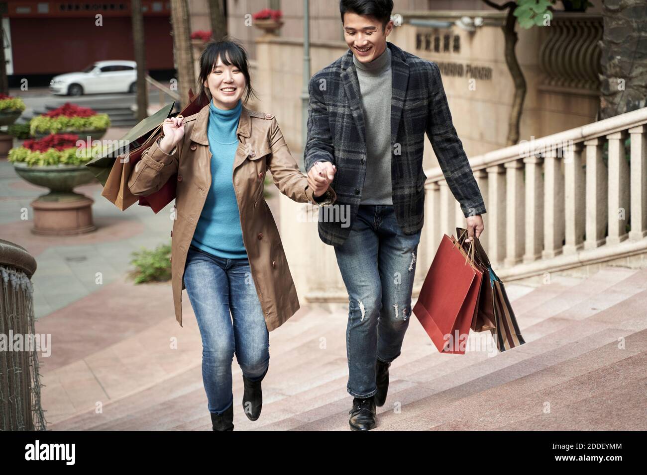 young asian couple carrying shopping bags holding hands walking on ...