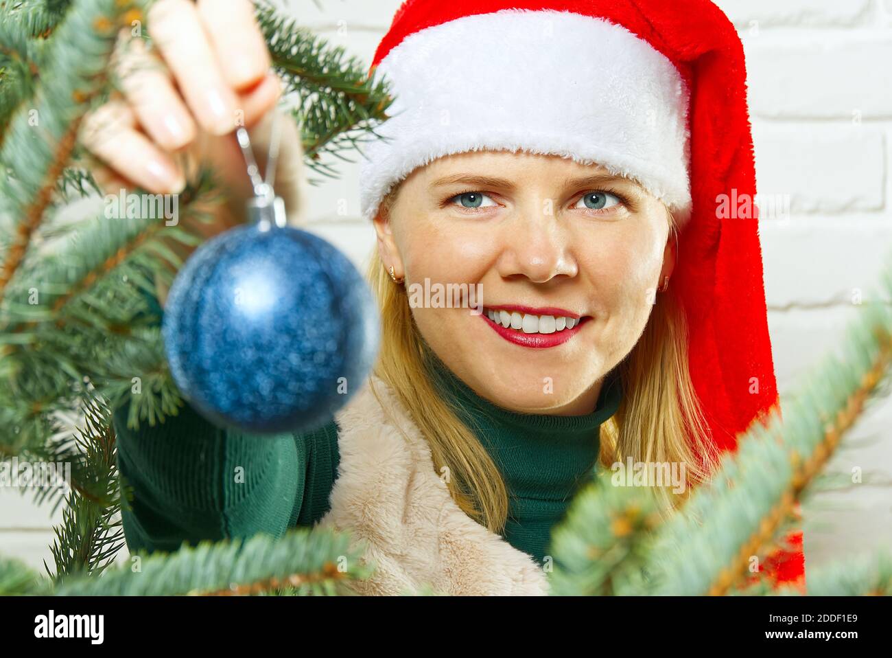 Blond pretty woman decorating christmas tree with blue ornaments decor ...