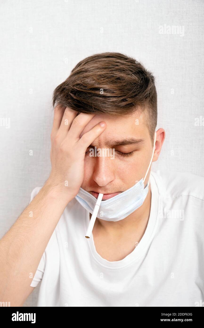 Sad Young Man in a Flu Mask with a Cigarette on the White Wall ...