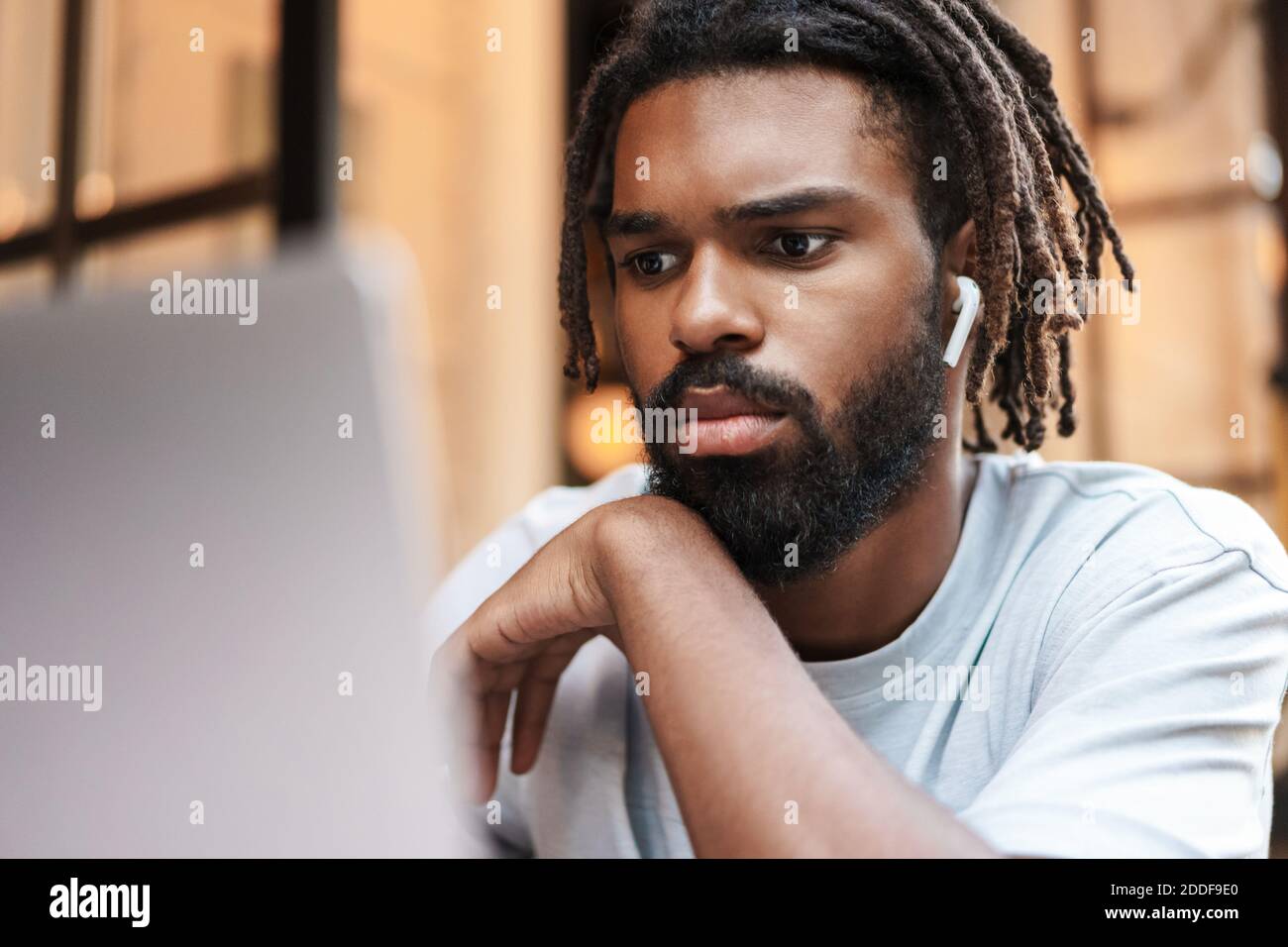 Focused african american guy in earphones working with laptop while ...