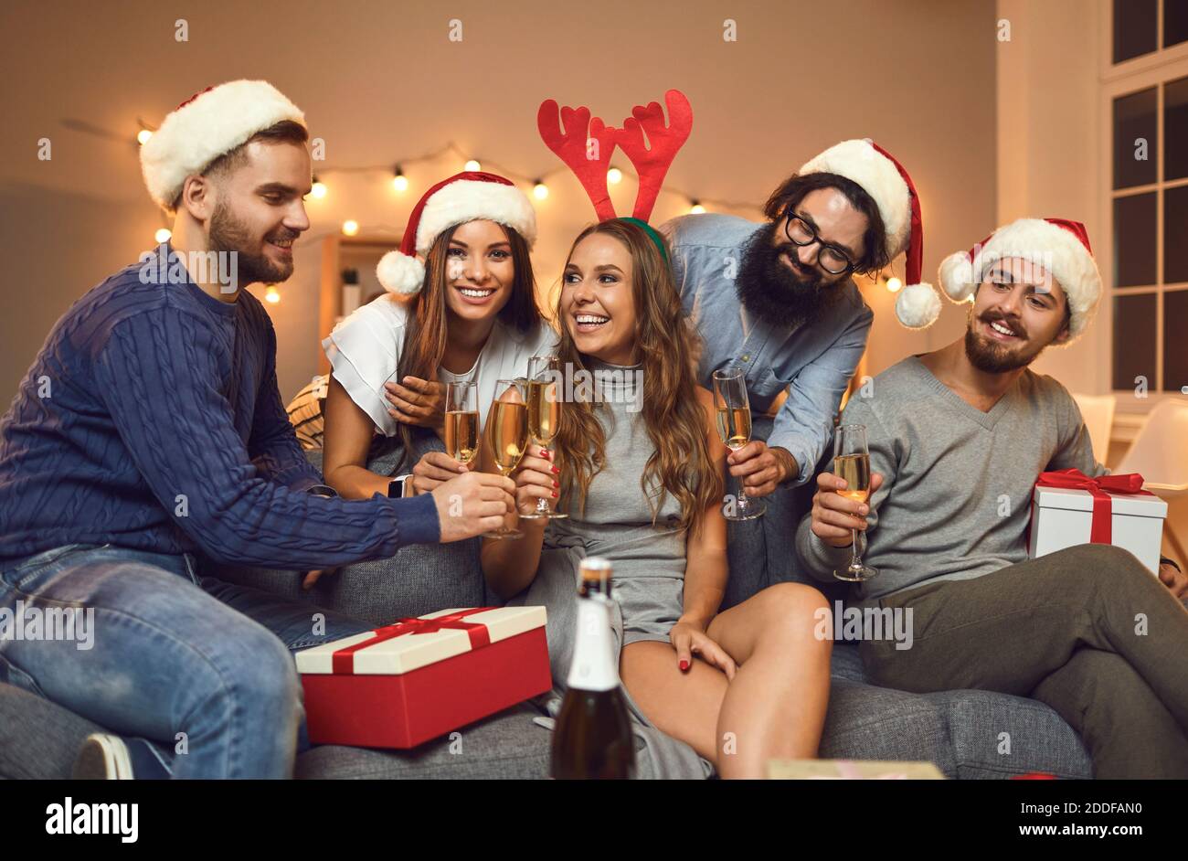 Group of smiling friends in holiday caps and accessories feasting ...