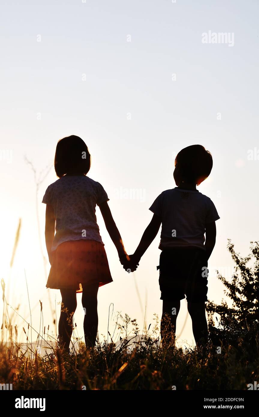 Two children, male and female standing against the sun, sunset, romance ...