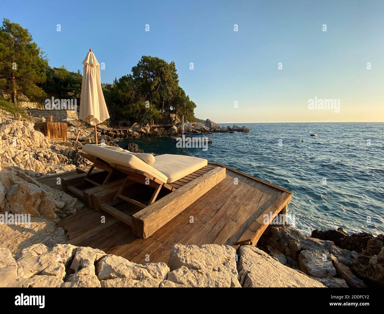 Sunbed and sun shade on a wooden sun deck on the rocks, next to wavy ...