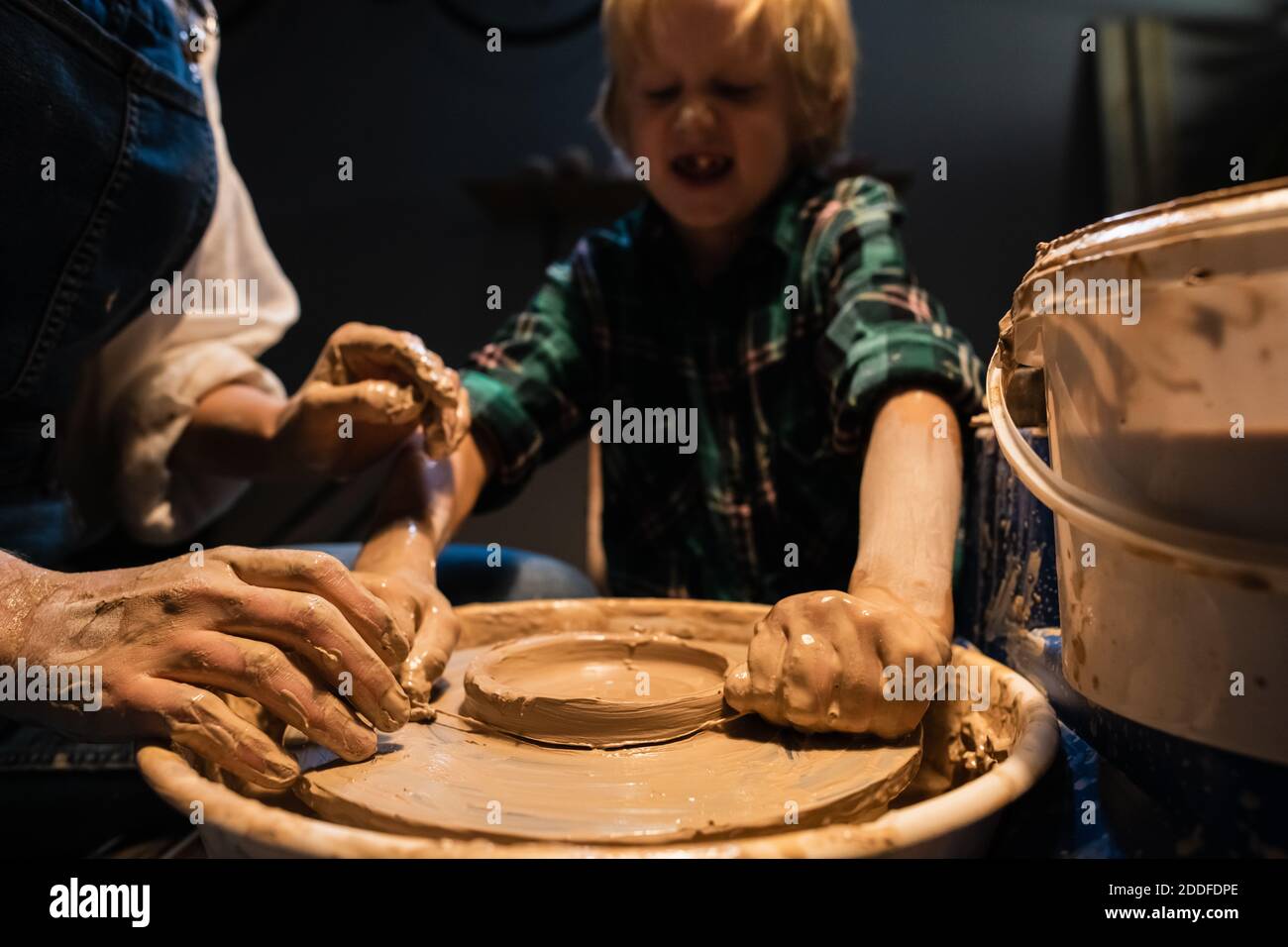a small boy sculpts a plate out of clay under the supervision of a ...