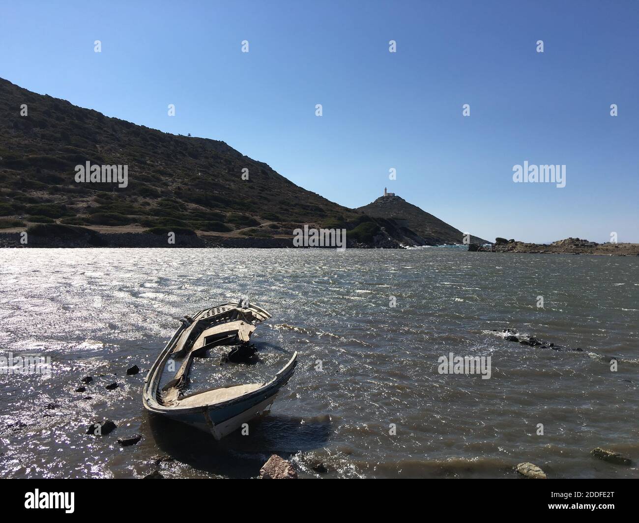 Wrecked boat on the Mediterranean sea water, mountains at the back and ...