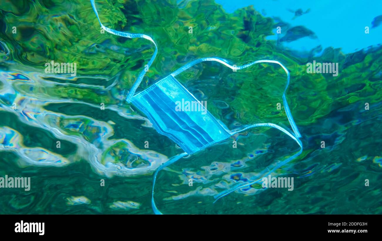 Discarded mask with ties slowly drifts under surface of water ...