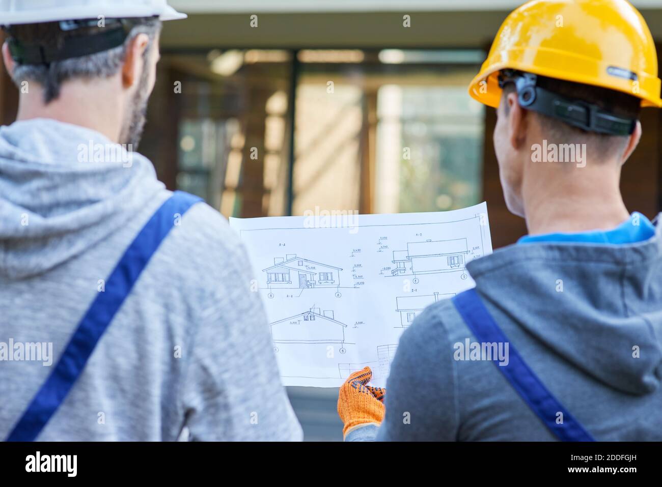 Close up of two builders standing outdoors with an open blueprint ...
