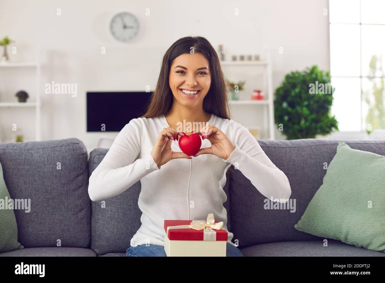 Happy woman sitting on couch with Valentine present on her lap, holding ...