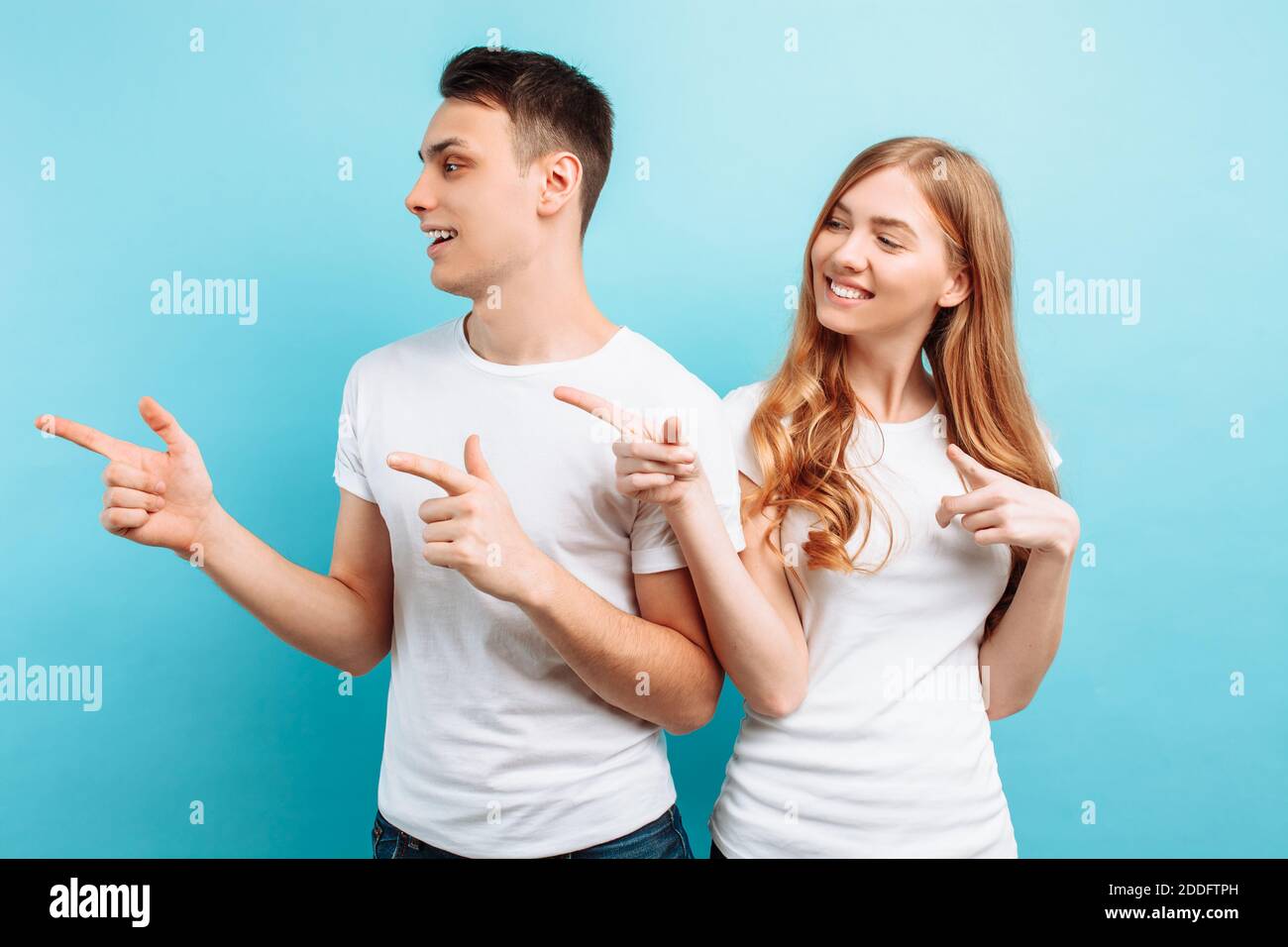 Portrait of a cheerful young couple, man and woman pointing fingers at ...