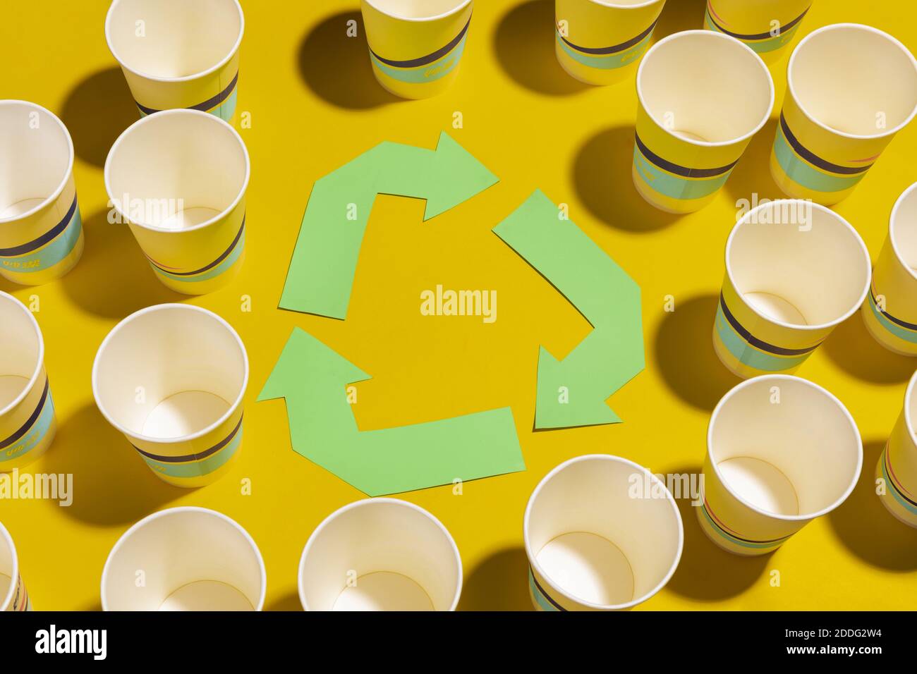 A recycling sign and paper cups on yellow surface Stock Photo - Alamy