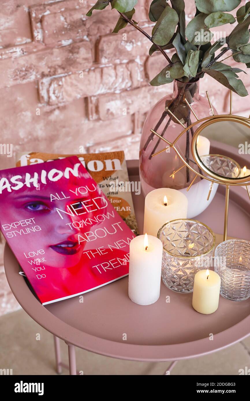Burning candles, fashion magazines and mirror on table in room Stock ...
