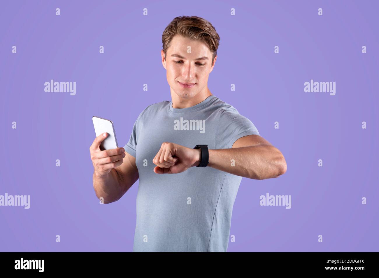 Active millennial guy with modern smartwatch and cellphone over violet ...