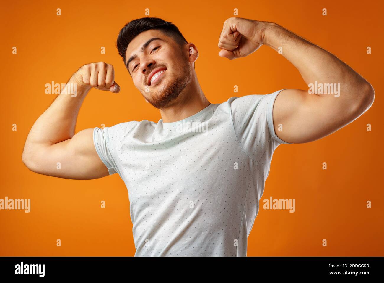 Positive smiling young man showing his strong arms against yellow ...
