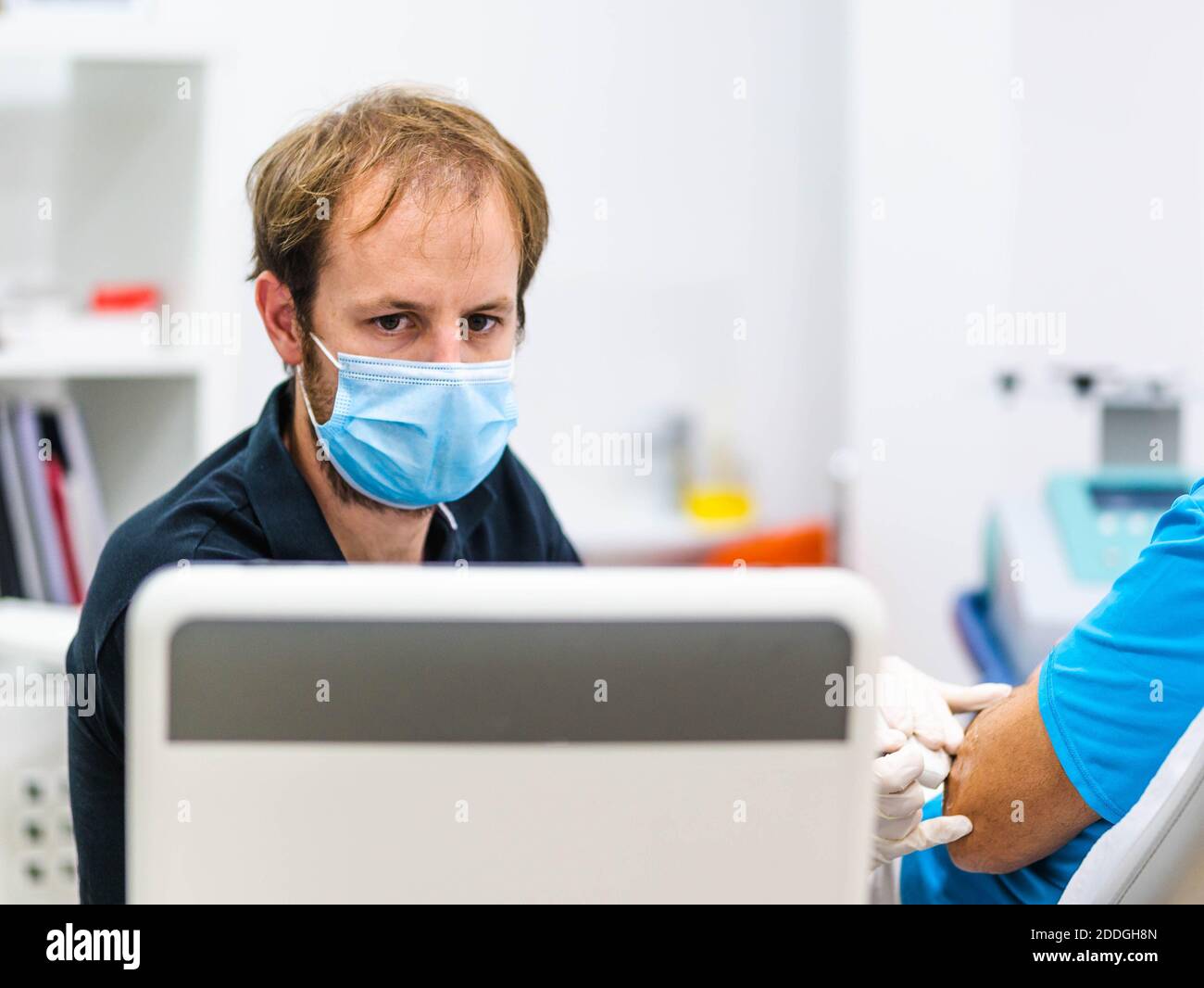 man in medical mask focusing on computer monitor while examining arm of ...