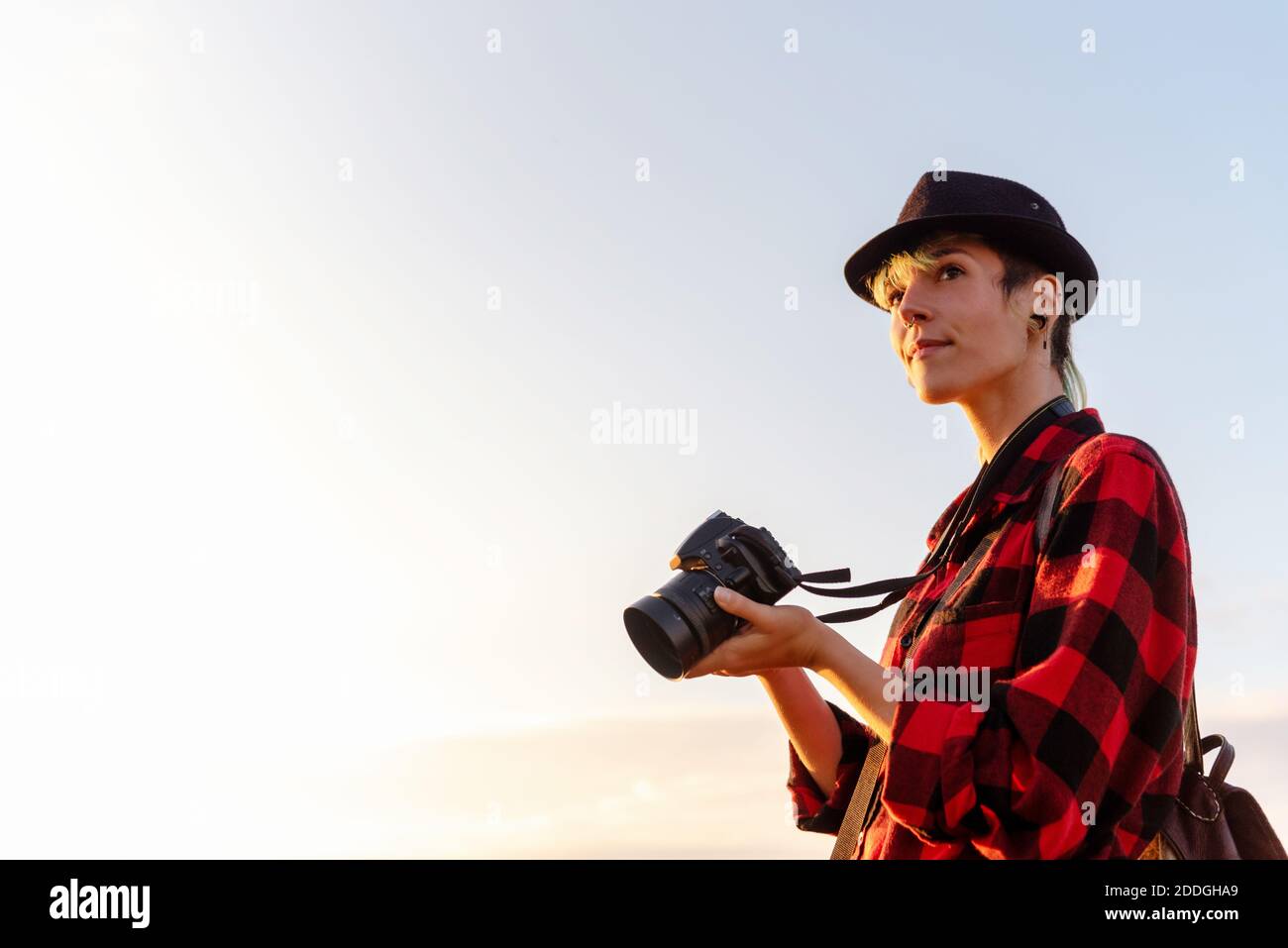 Side view of androgynous female traveler with professional photo camera ...