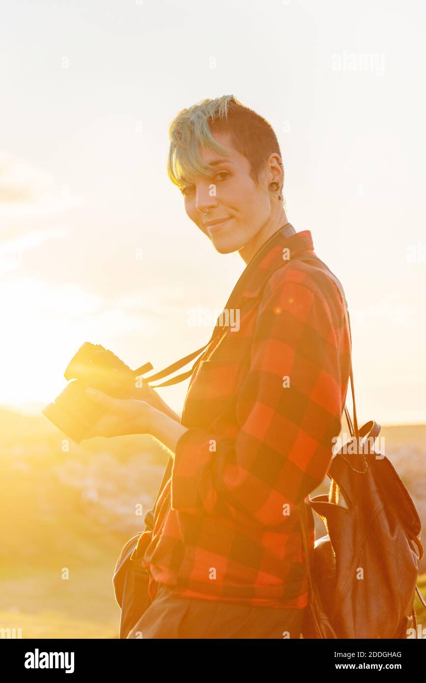 Side view of androgynous female traveler with professional photo camera ...